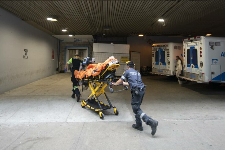 Paramedics wheel a gurney into the back of a hospital. Several parked ...
