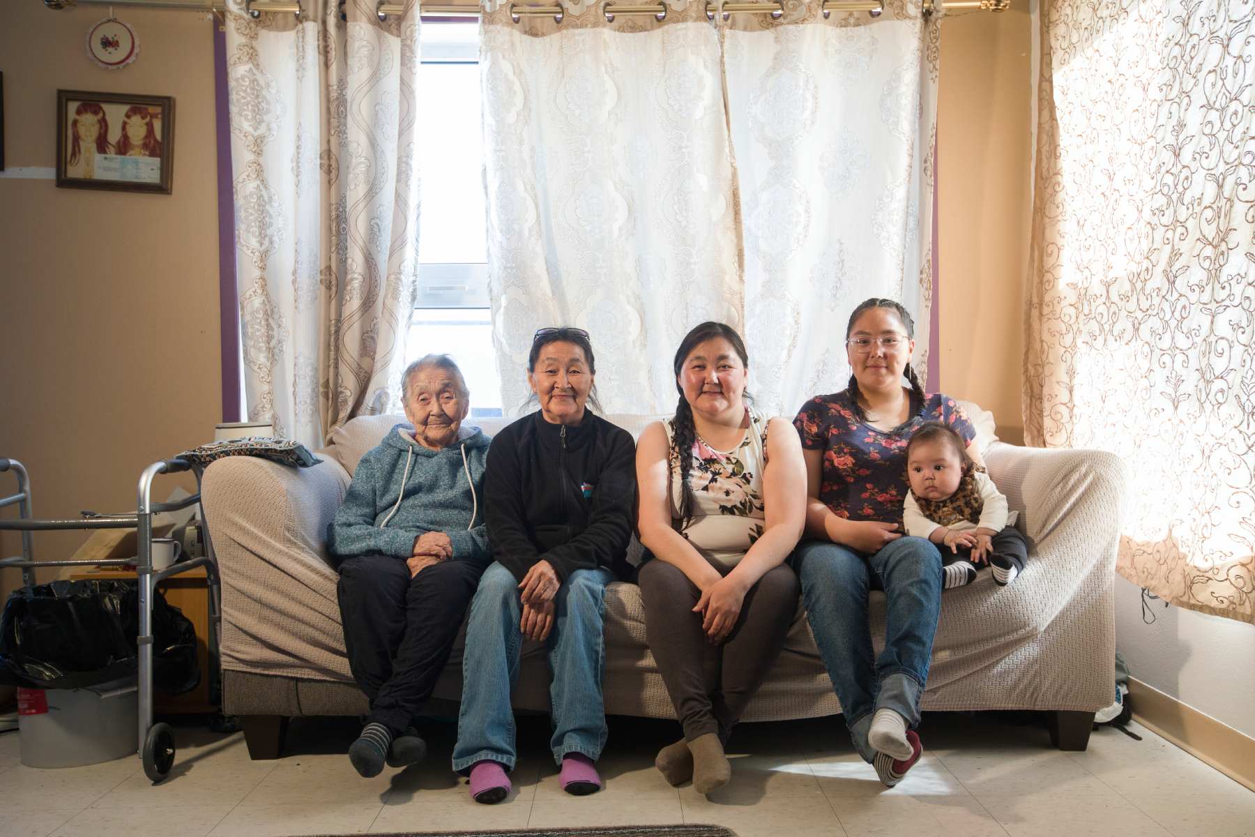 Photo of four people sitting together on a sofa, arranged by age. The ...