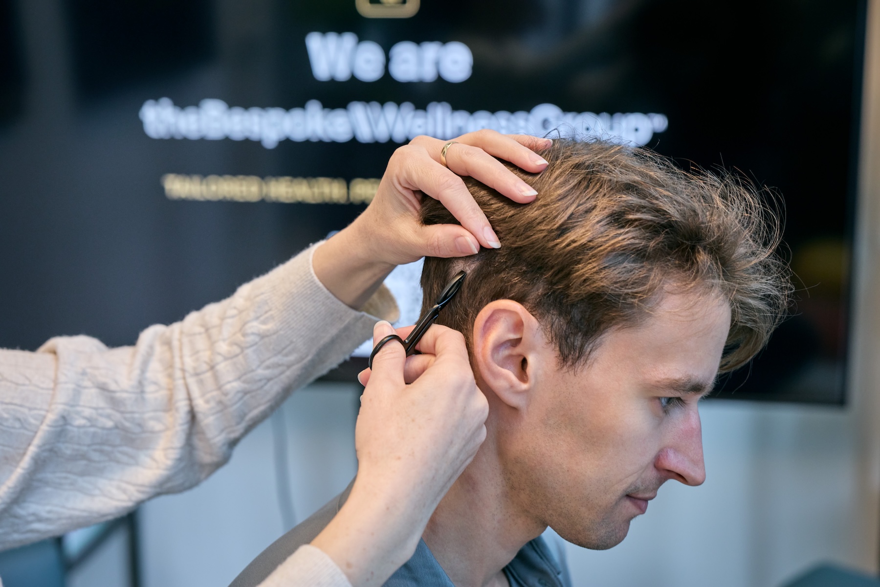 Photo of a man with short hair in profile. Hands from an offscreen ...