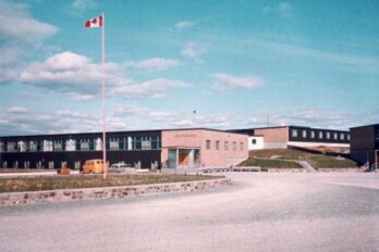 An old colour photograph showing a blue sky over several low school ...