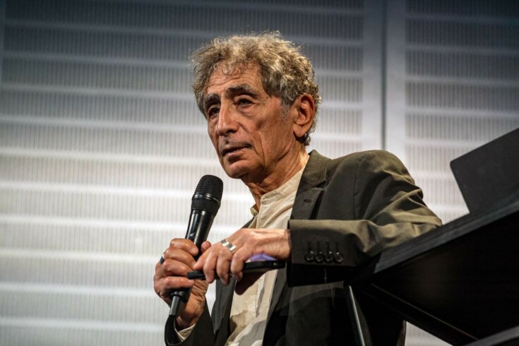 Photo of author Gabor Maté, a man with grey hair, speaking into a ...