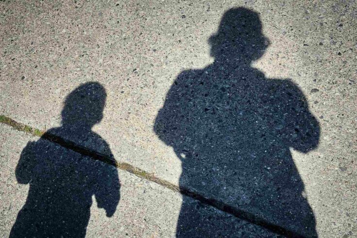 Photo shows the shadow of a man and a child, with a line on the road ...