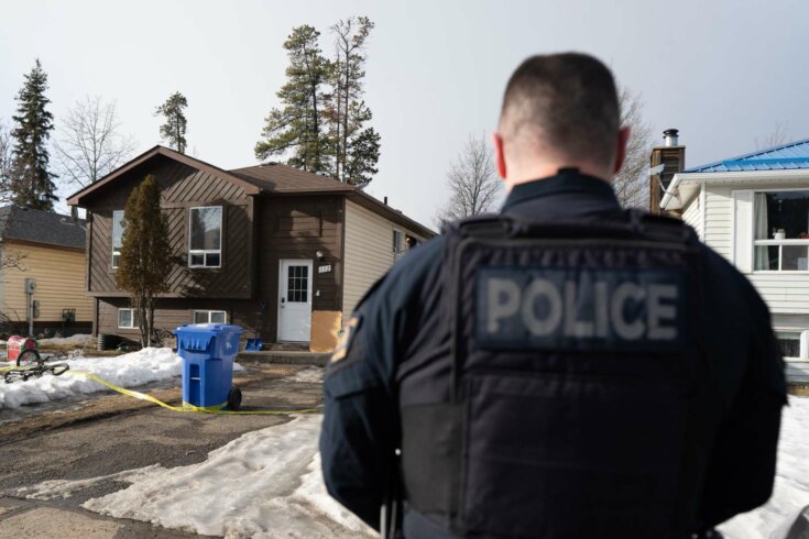 Photo of the back of a police officer standing outside of a house.