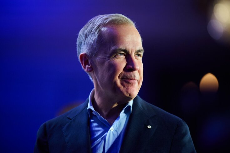 Photo of Prime Minister Mark Carney smiling in front of a blurry, dark ...