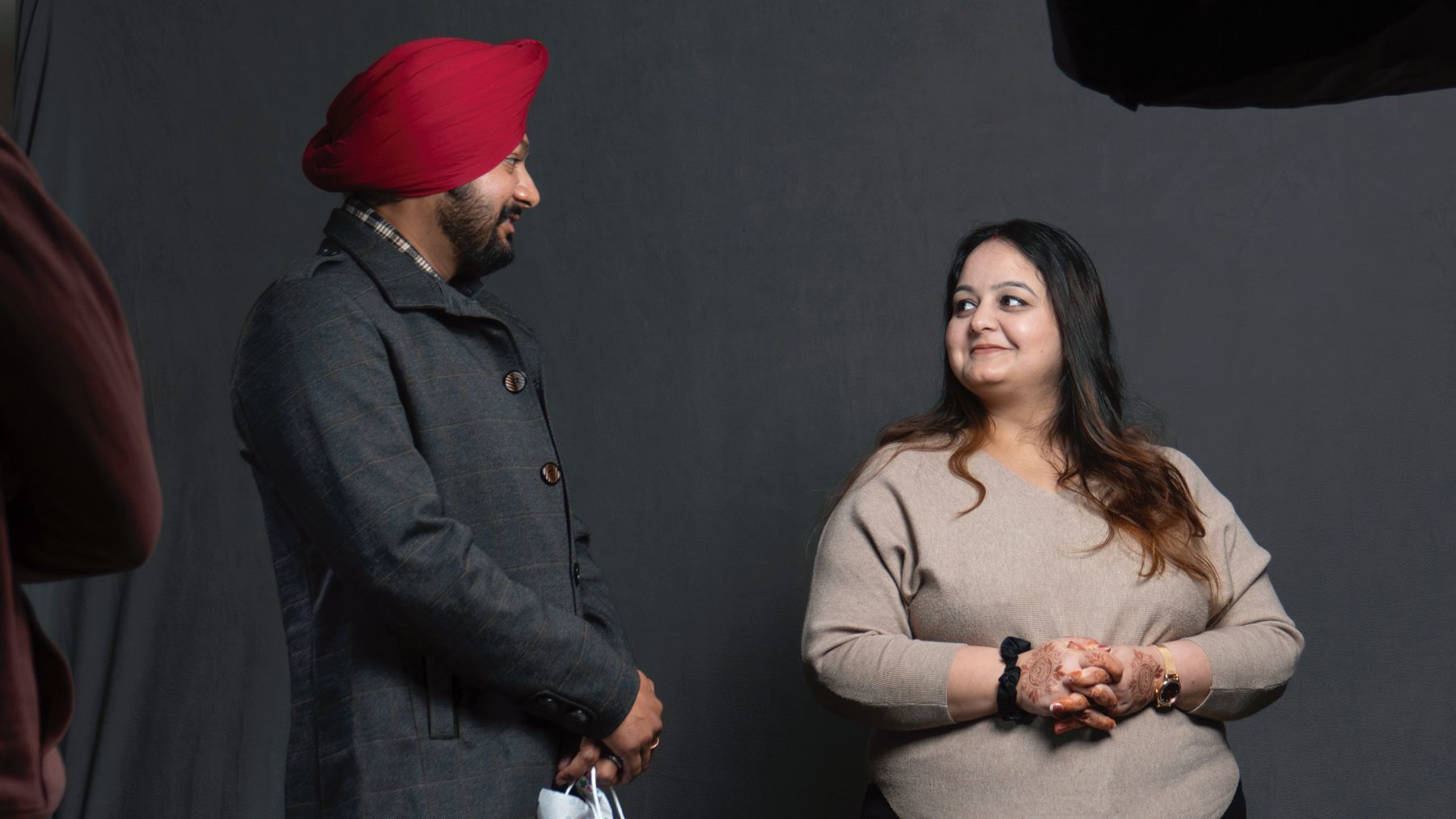 Photo shows a man in a red turban and black coat and a woman in beige ...